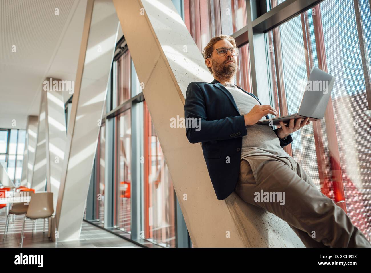 Businessman holding laptop leaning on column in building Stock Photo ...
