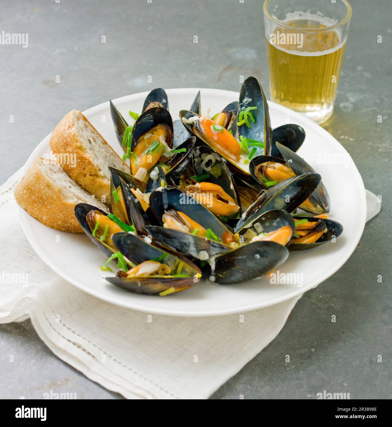 A pint of muscles in their shells, in a white bowl with crusty French ...