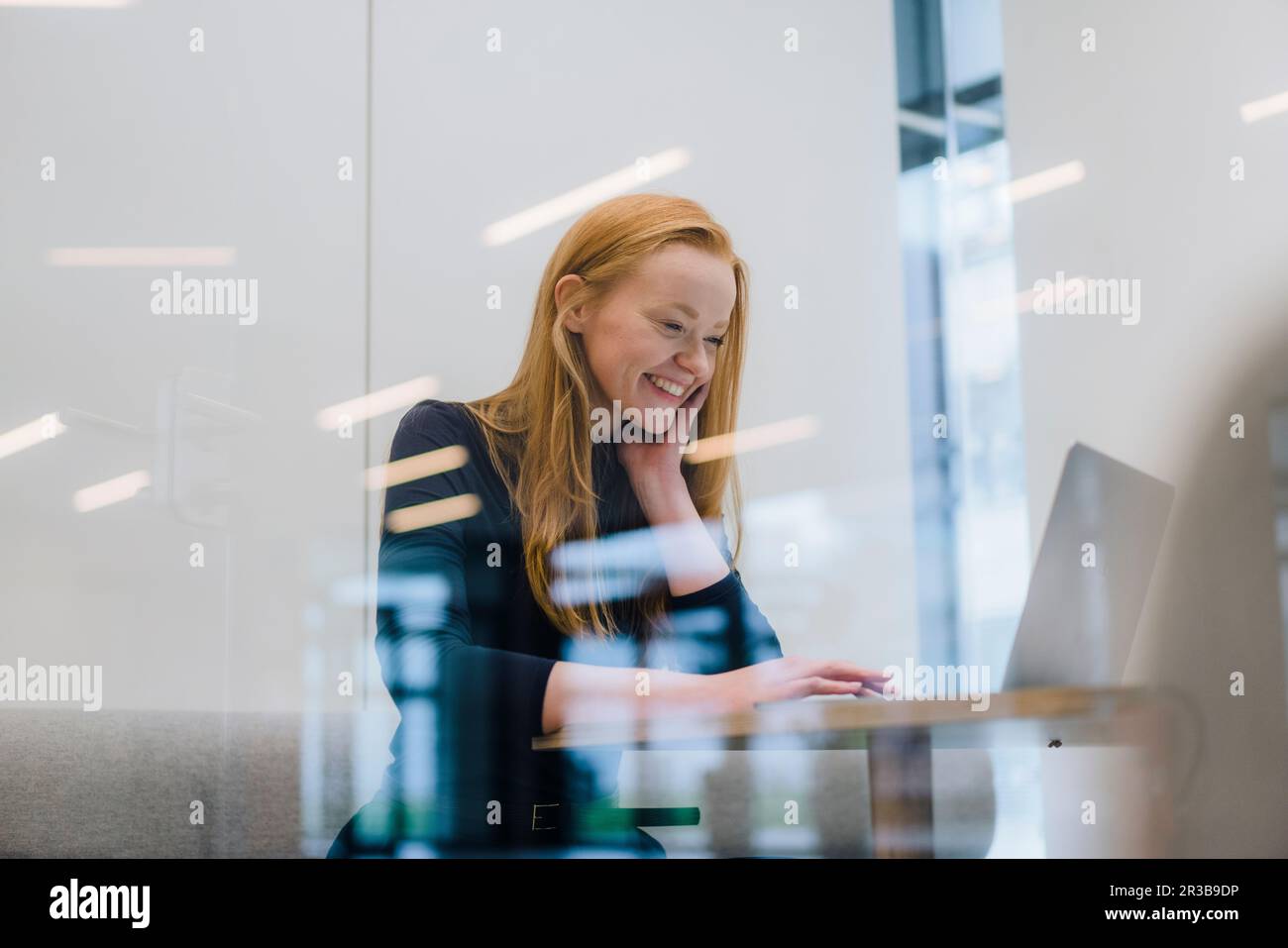 Smiling businesswoman working on laptop sitting in office cubicle Stock ...