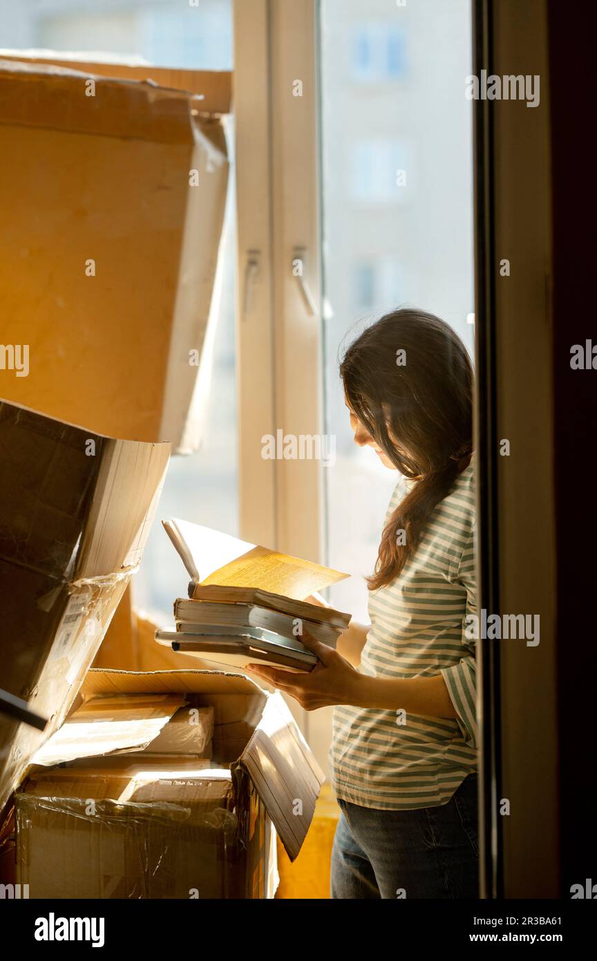 Woman packing books in carton seen through window Stock Photo - Alamy