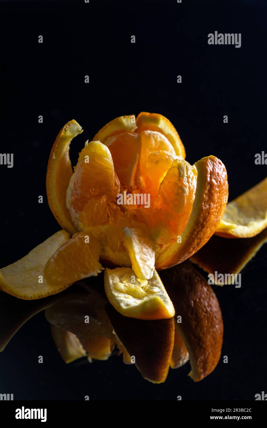 A peeled orange broken into segments against a black background Stock ...