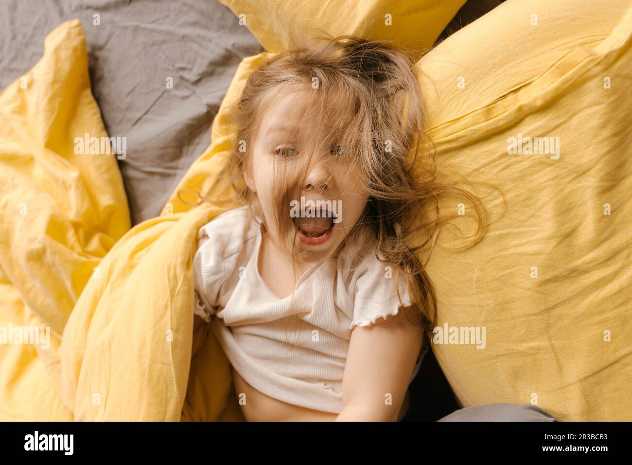Blond girl screaming on bed by pillow at home Stock Photo - Alamy
