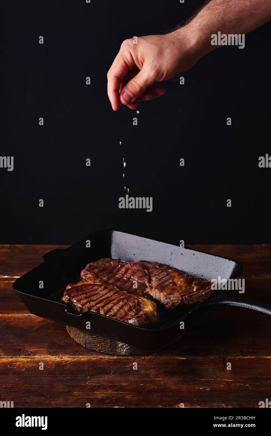 Male hands adding salt to beef steak on grill Stock Photo - Alamy