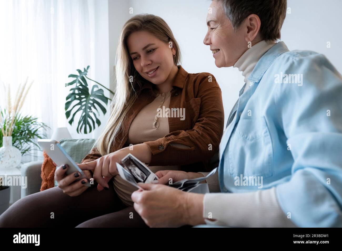 Pregnant woman sharing ultrasound scan with mother through smart phone ...
