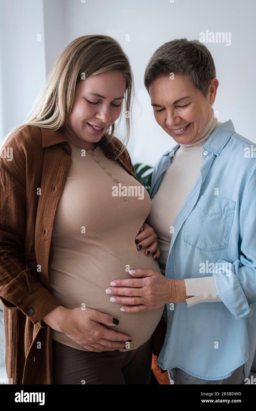 Smiling senior woman touching belly of pregnant daughter at home Stock ...
