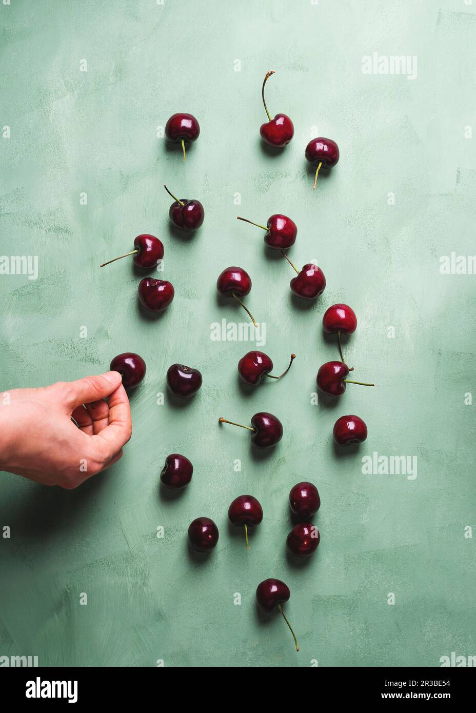 Ripe cherries over green background with female hand taking one cherry ...