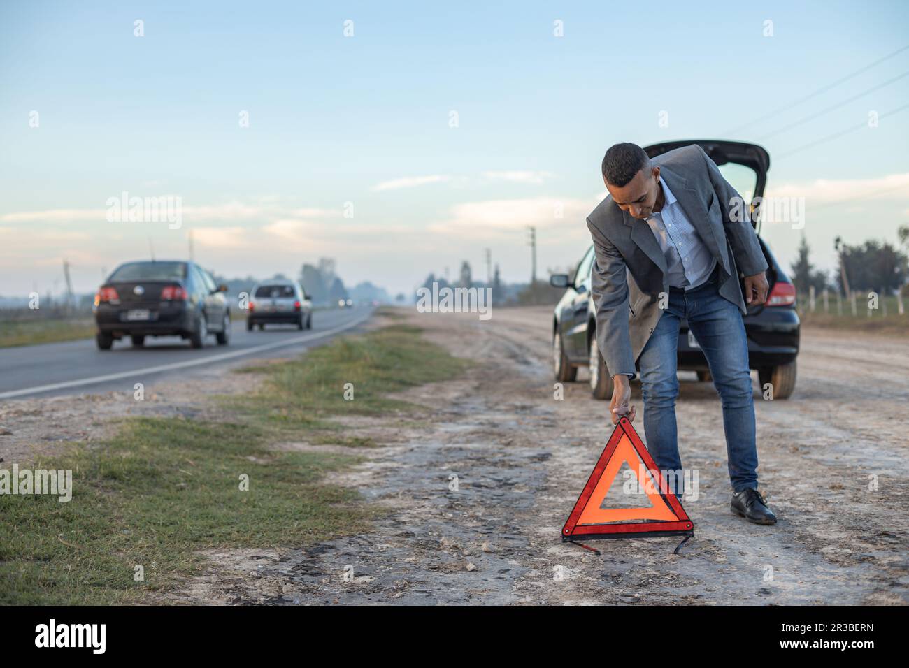 Young Latino man placing a warning triangle behind a broken down car ...