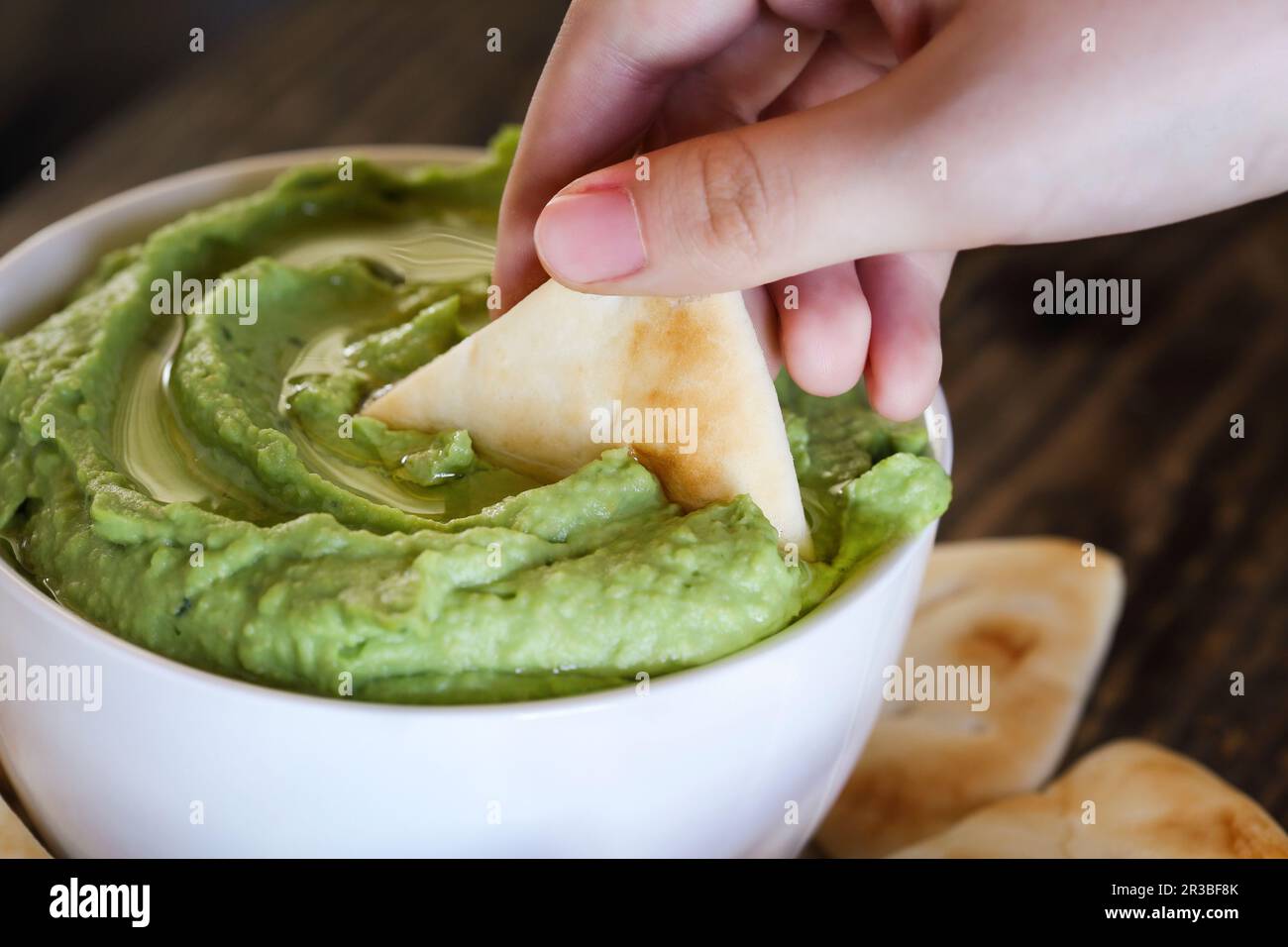 Woman's hand dipping pita bread into vegan avocado hummus Stock Photo ...