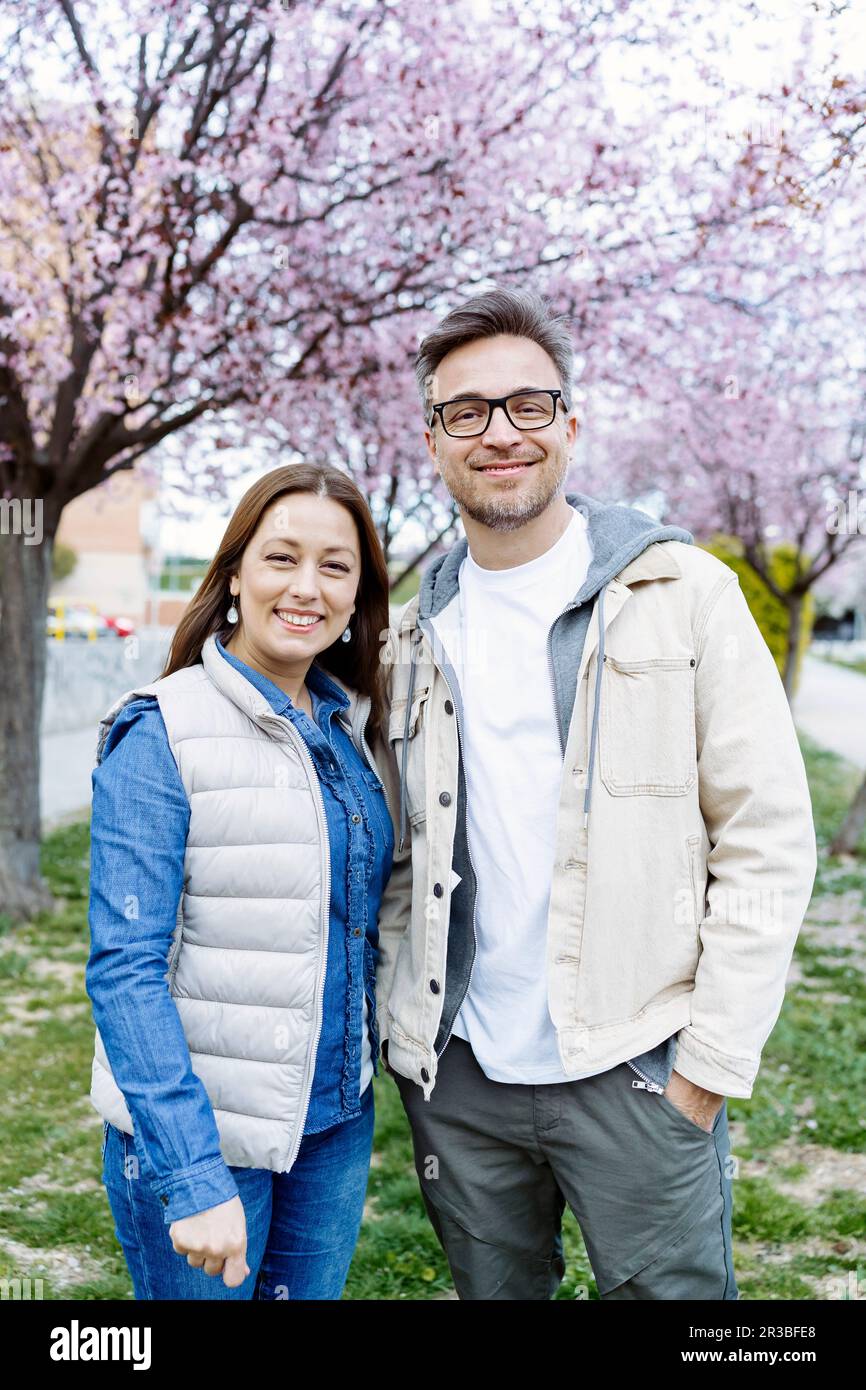 Smiling couple standing together in front of cherry blossom tree Stock ...