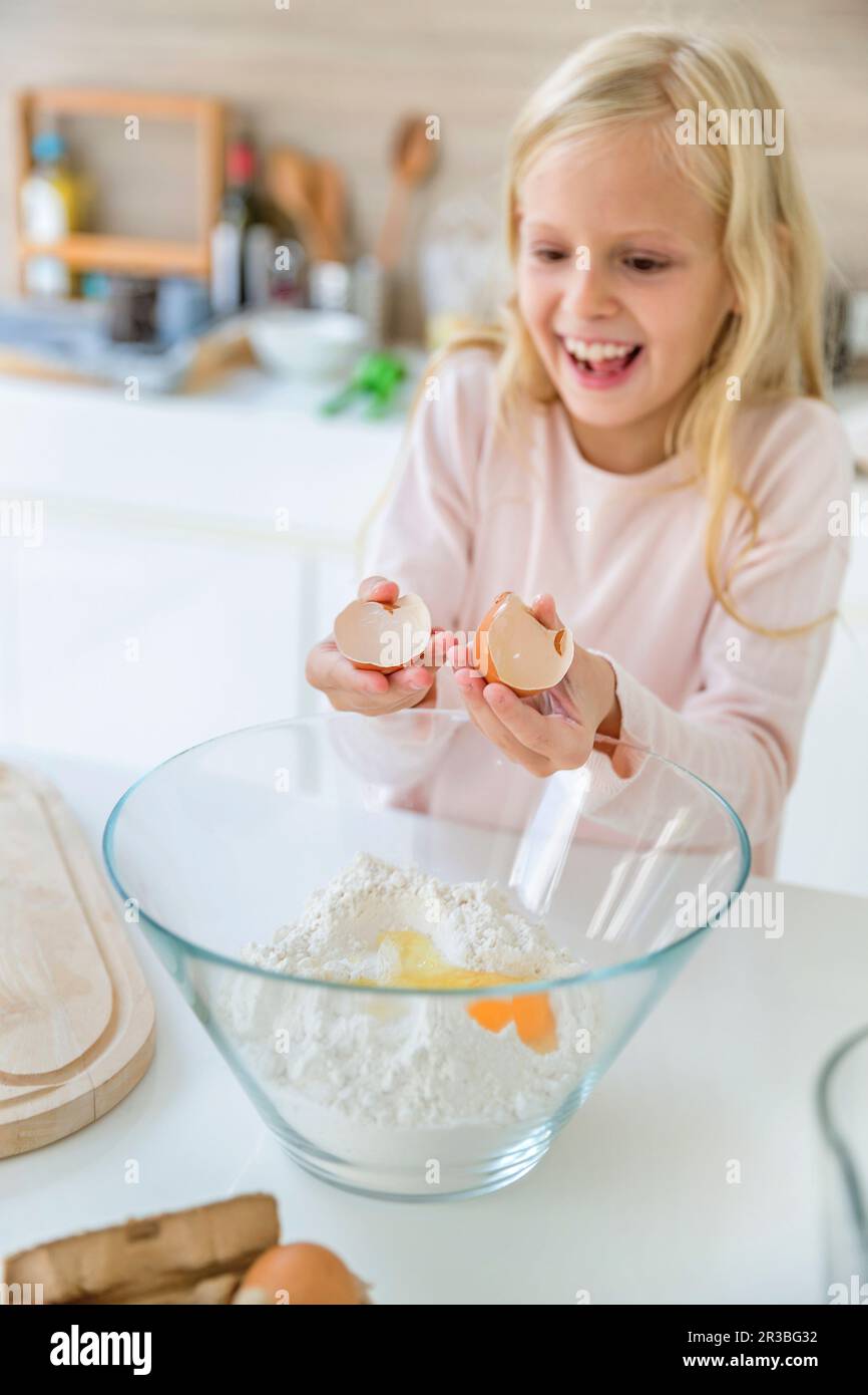 Happy girl breaking eggs in flour in kitchen at home Stock Photo - Alamy