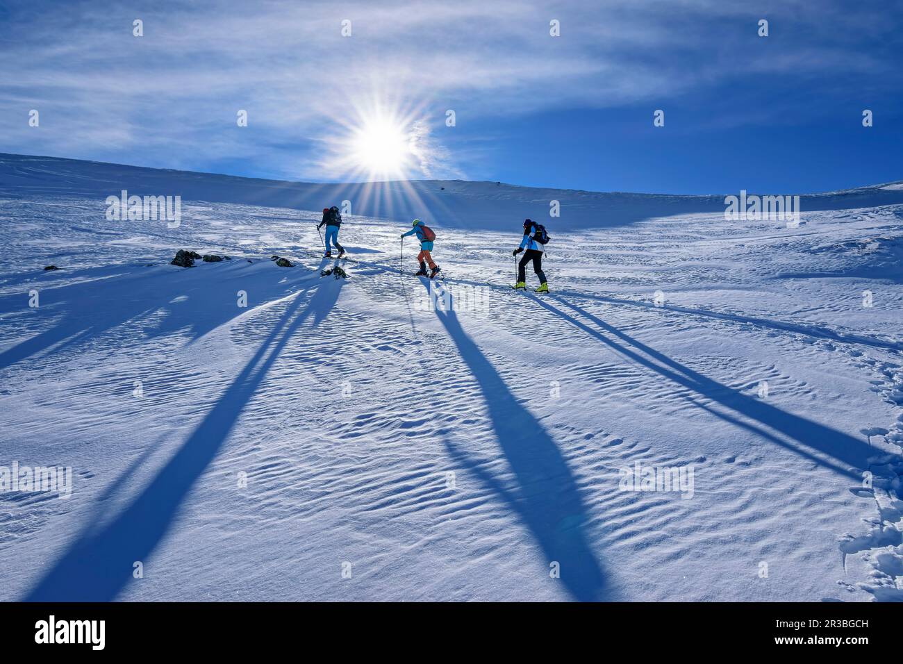Austria, Tyrol, Sun shining over three skiers traveling through snow in ...