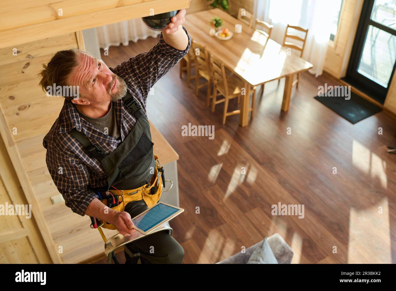 Mature fitterman in coveralls and checkered shirt fixing or adjusting ...