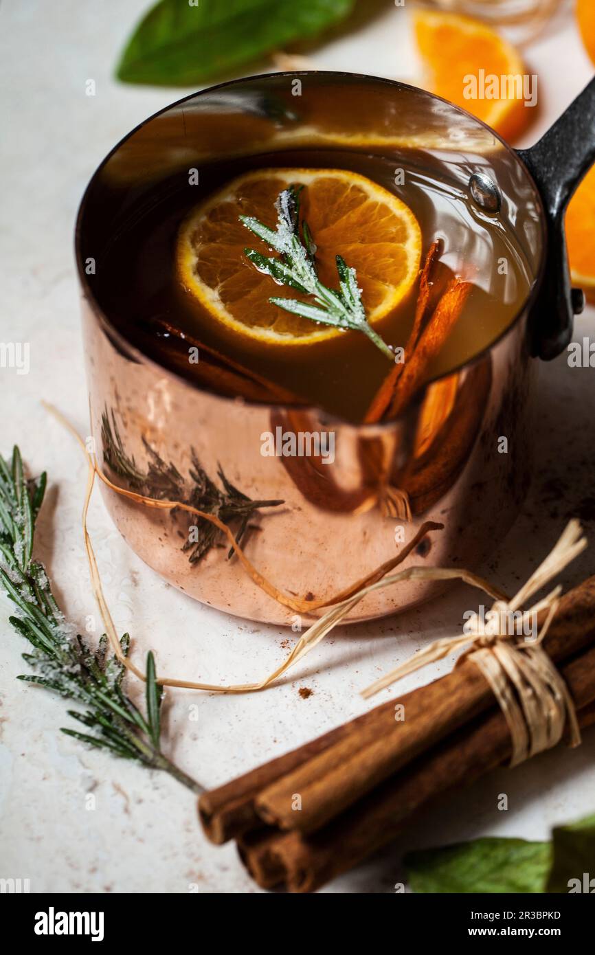 Apple cider heated in an antique copper pot, with oranges with leaves ...