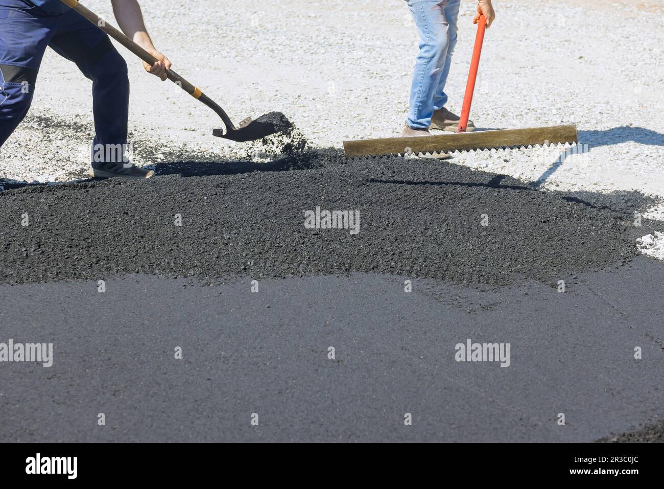Work laying asphalt on road pavement is accompanied by men shovelling ...