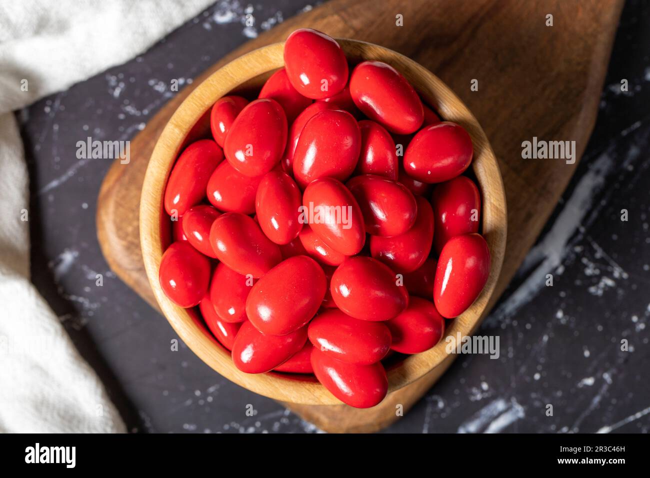 Chocolate almond dragee. Red chocolate dragee in wooden bowl on dark ...