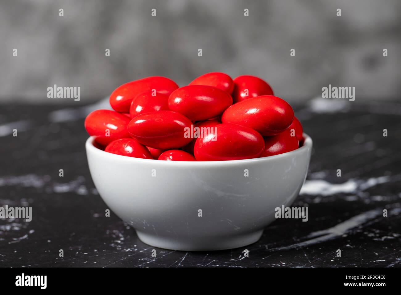 Chocolate almond dragee. Red chocolate dragee in ceramic bowl on dark ...