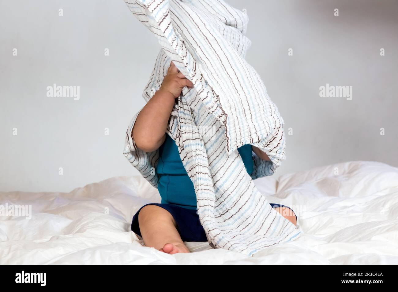 Small Caucasian boy playing under a striped blanket on white bedding ...