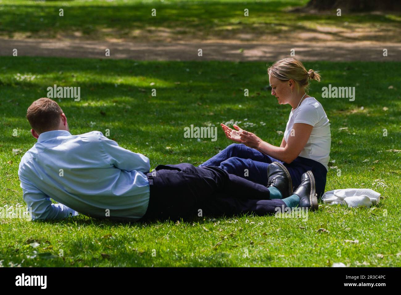 London UK. 23 May 2023 A man and woman relaxing in the warm sunshine in ...