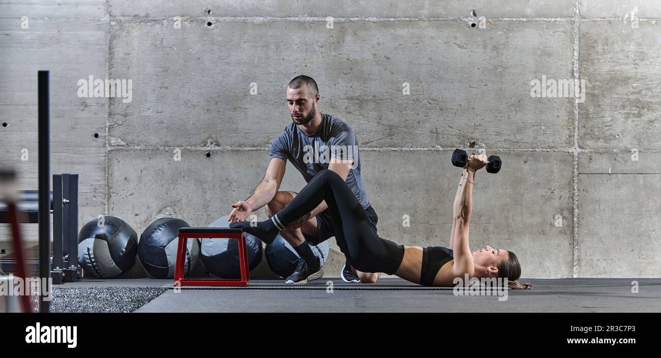 A muscular man assisting a fit woman in a modern gym as they engage in ...