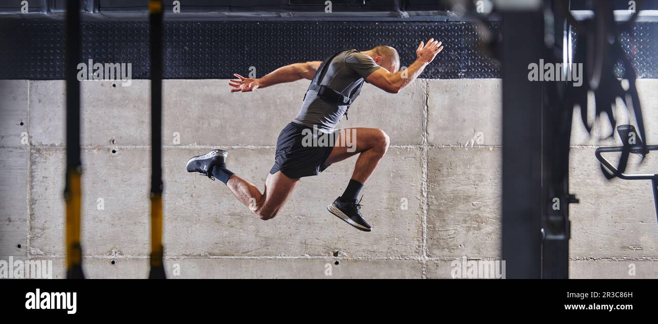 A muscular man captured in air as he jumps in a modern gym, showcasing ...