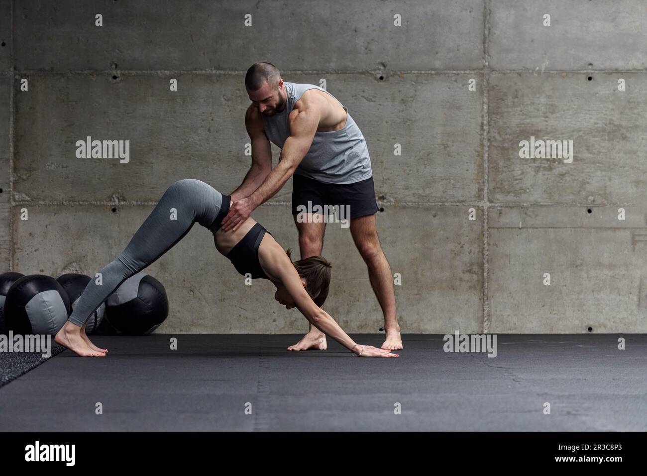 A muscular man assisting a fit woman in a modern gym as they engage in ...