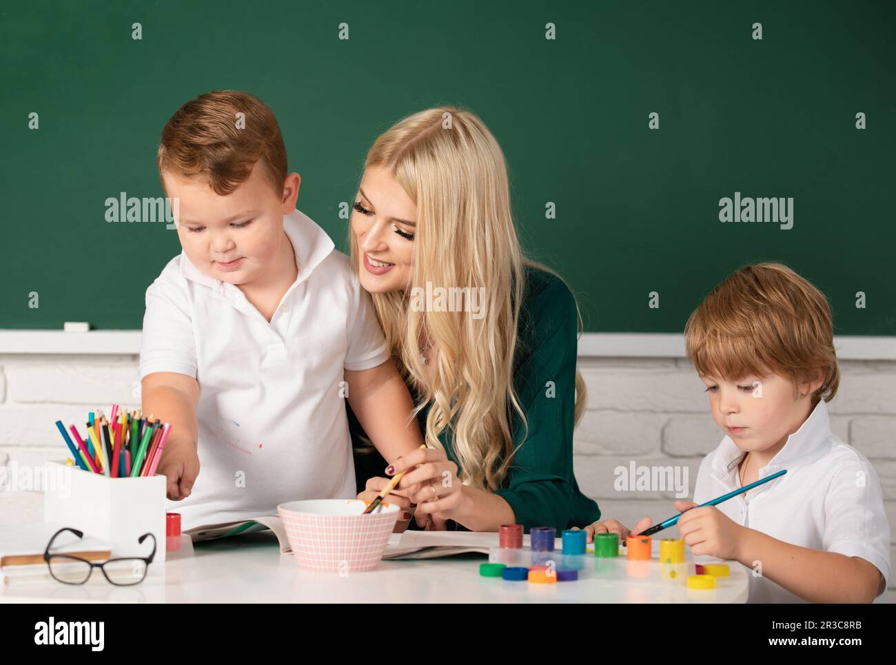 Teacher helping school kids in classroom at school. Children drawing in ...