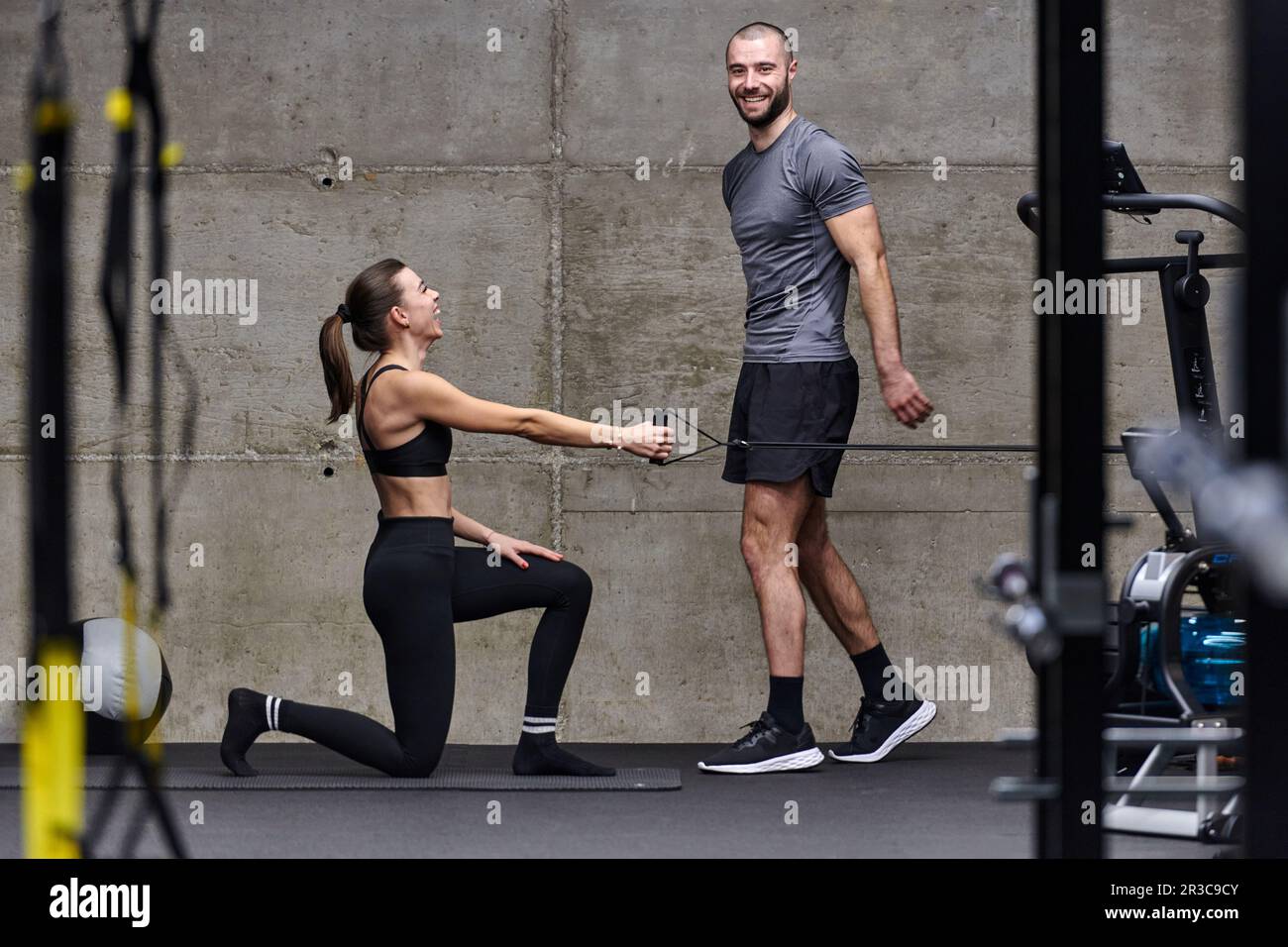 A muscular man assisting a fit woman in a modern gym as they engage in ...