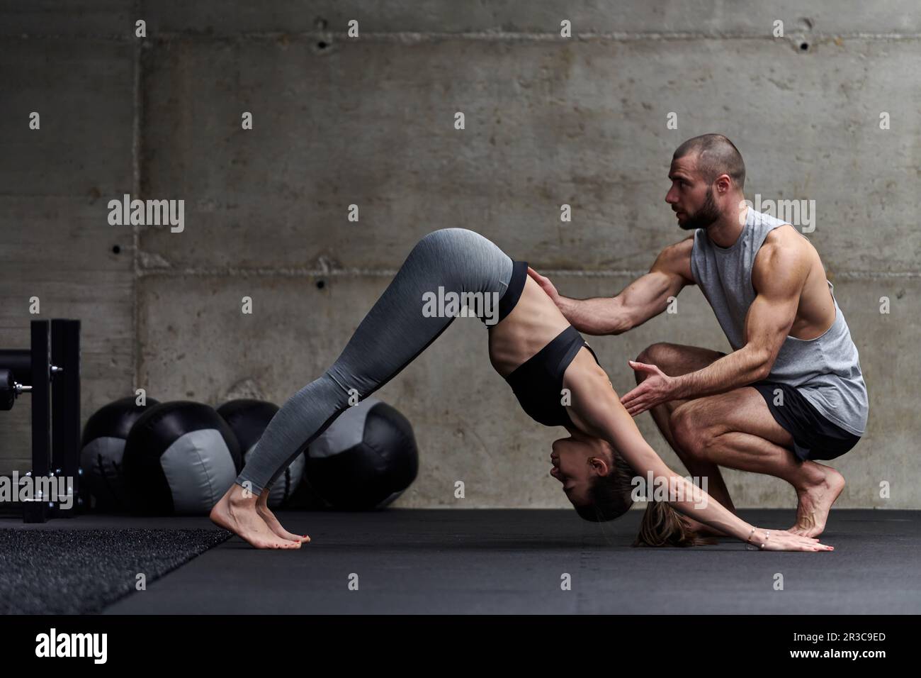A muscular man assisting a fit woman in a modern gym as they engage in ...