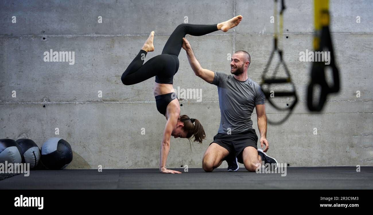 A muscular man assisting a fit woman in a modern gym as they engage in ...