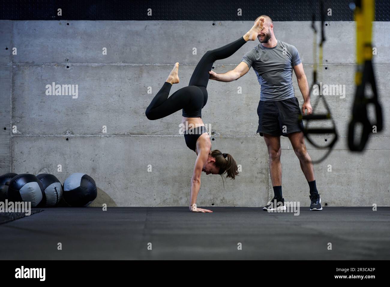 A muscular man assisting a fit woman in a modern gym as they engage in ...