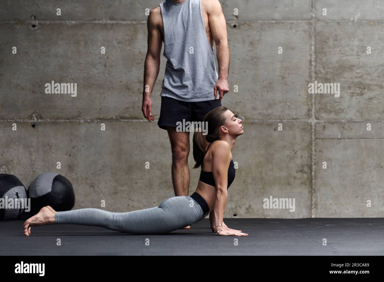 A muscular man assisting a fit woman in a modern gym as they engage in ...