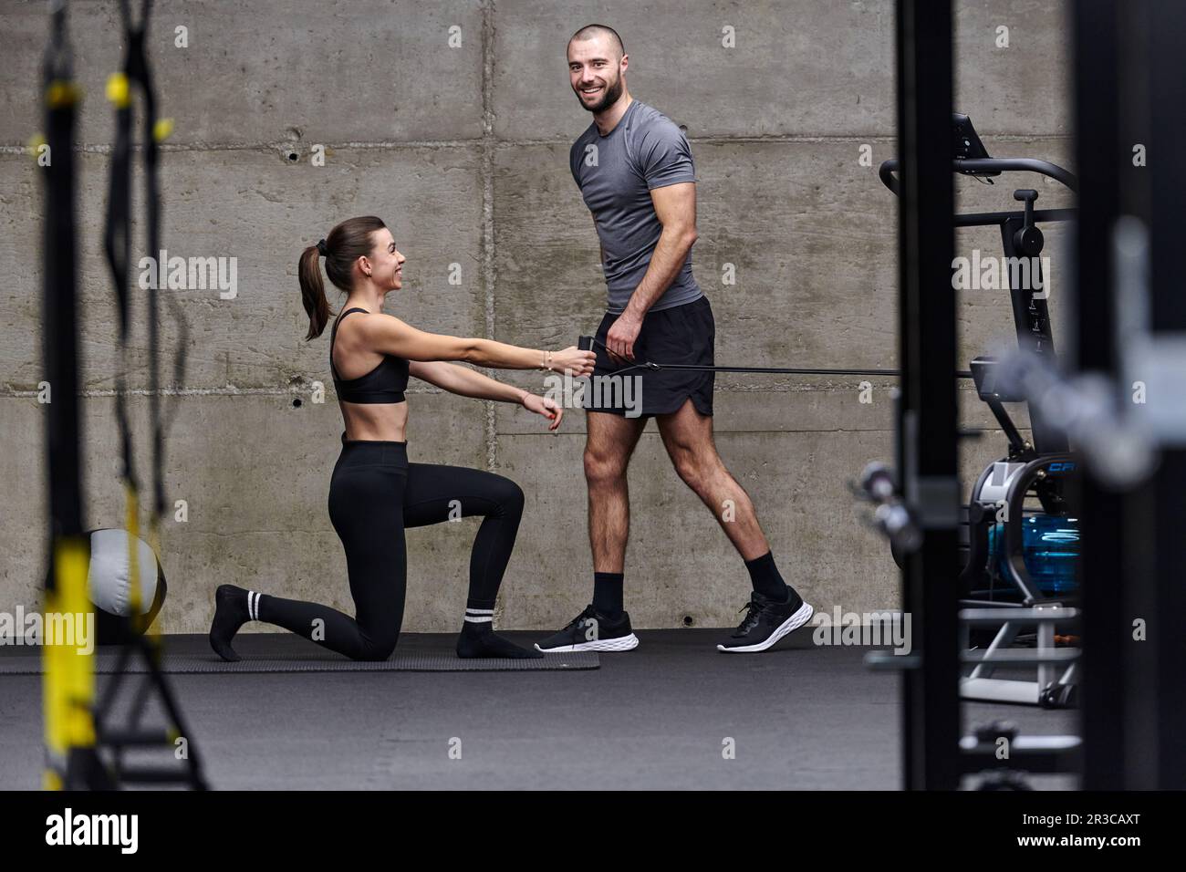 A muscular man assisting a fit woman in a modern gym as they engage in ...