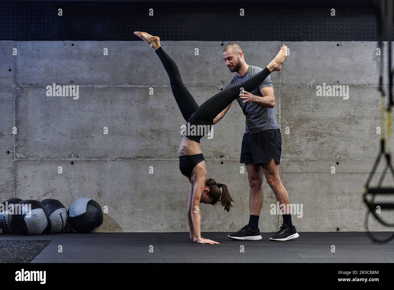 A muscular man assisting a fit woman in a modern gym as they engage in ...
