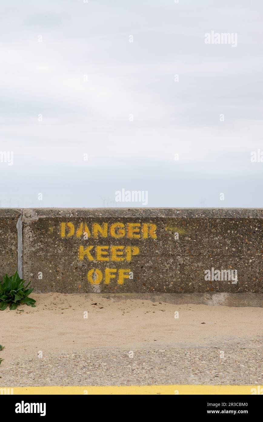 Seawall with warning sign painted onto the wall Stock Photo - Alamy