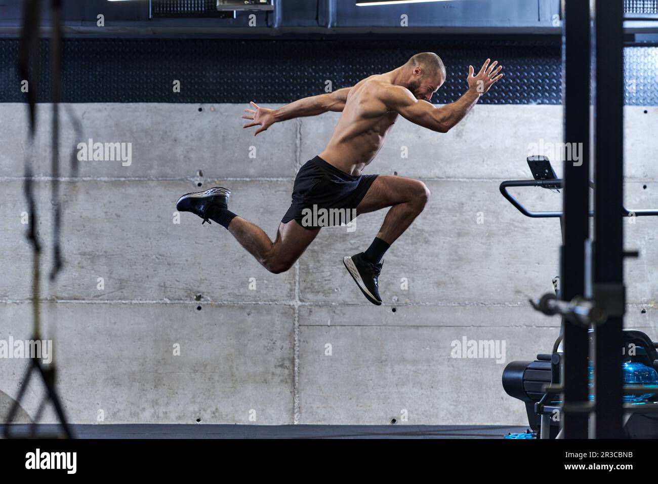 A muscular man captured in air as he jumps in a modern gym, showcasing ...