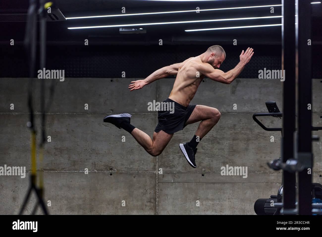 A muscular man captured in air as he jumps in a modern gym, showcasing ...