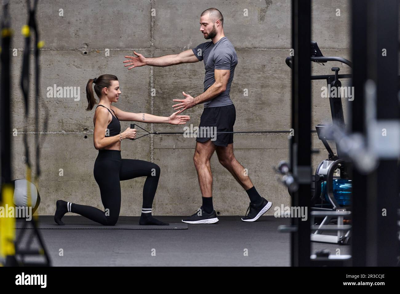 A muscular man assisting a fit woman in a modern gym as they engage in ...