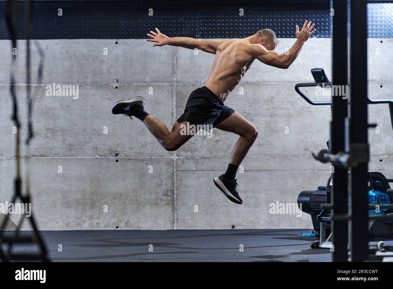 A muscular man captured in air as he jumps in a modern gym, showcasing ...