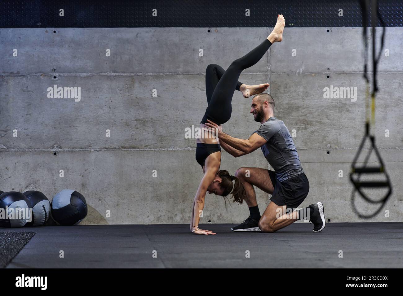 A muscular man assisting a fit woman in a modern gym as they engage in ...