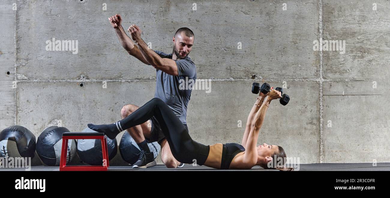 A muscular man assisting a fit woman in a modern gym as they engage in ...