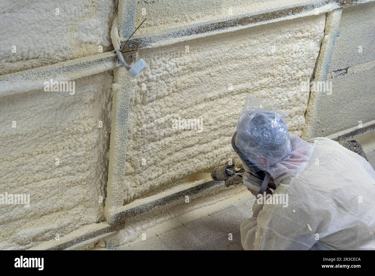 worker in a protective suit insulates the walls with polyurethane foam ...