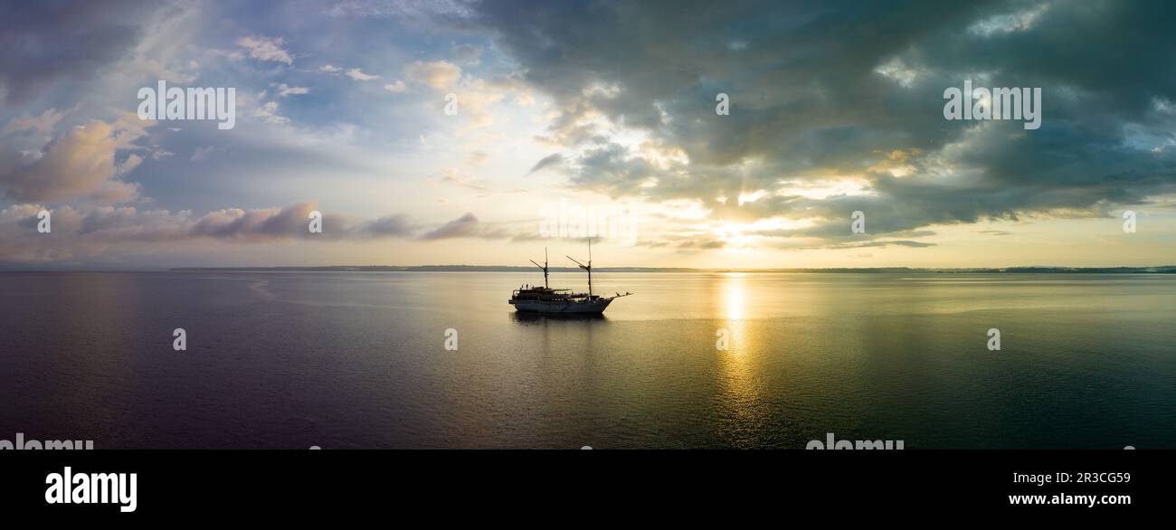 A tranquil sunrise illuminates a Phinisi schooner on the Pacific Ocean ...