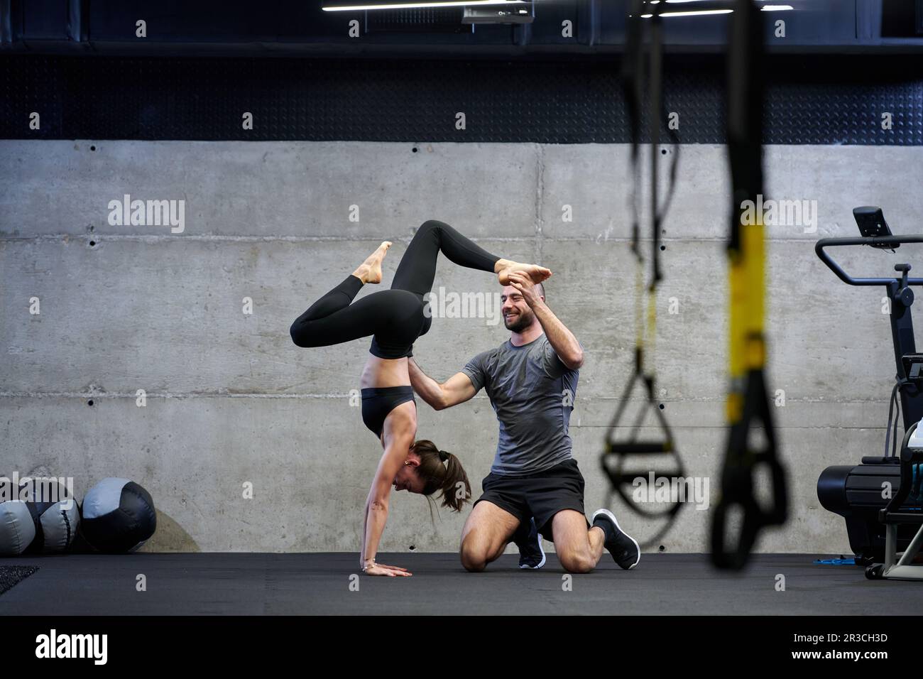 A muscular man assisting a fit woman in a modern gym as they engage in ...
