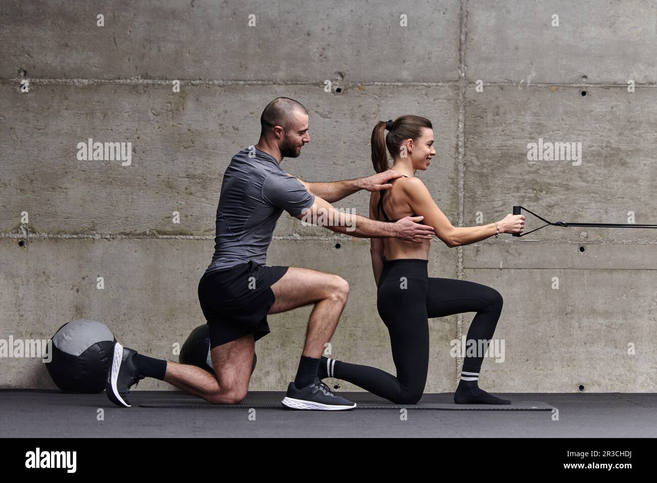 A muscular man assisting a fit woman in a modern gym as they engage in ...