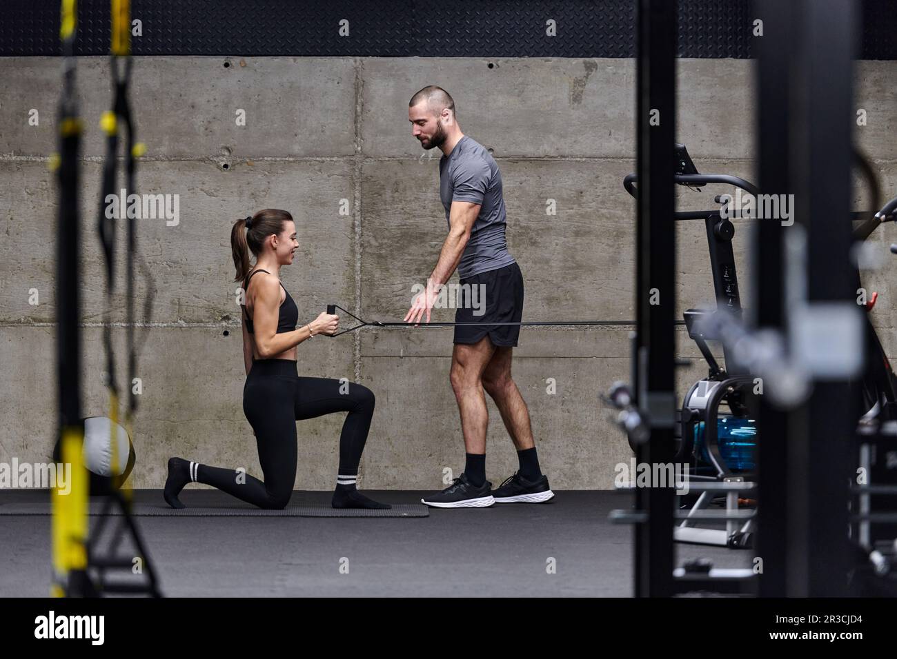 A muscular man assisting a fit woman in a modern gym as they engage in ...