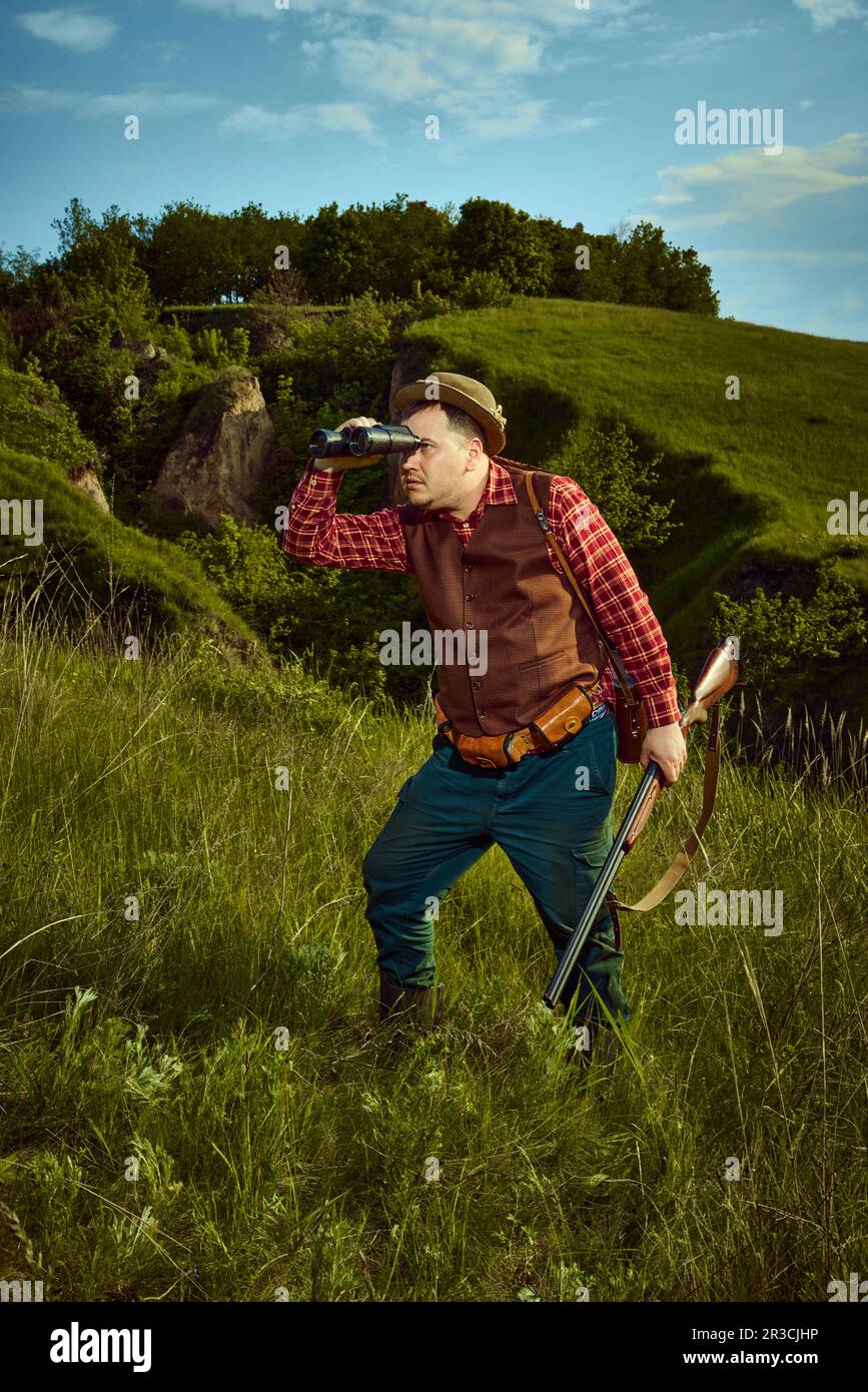 Handsome man, hunter in hat with feather holding weapon and binoculars ...