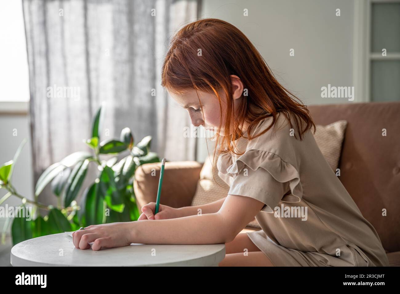 cute little preteen girl drawing with pen while sitting at desk at home ...