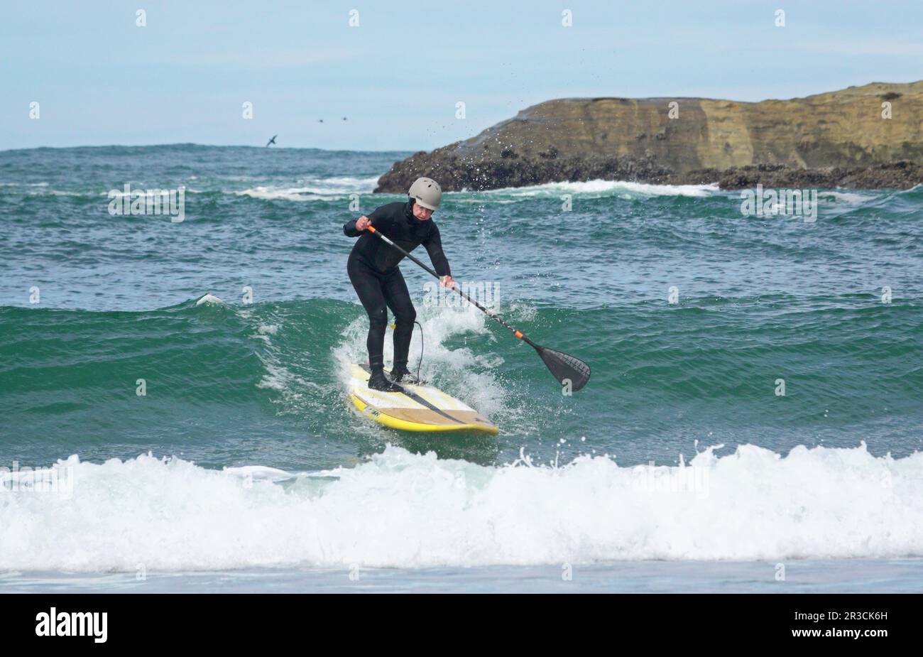 A standup paddleboarder rides the surf near Haystack Rock in Pacific ...