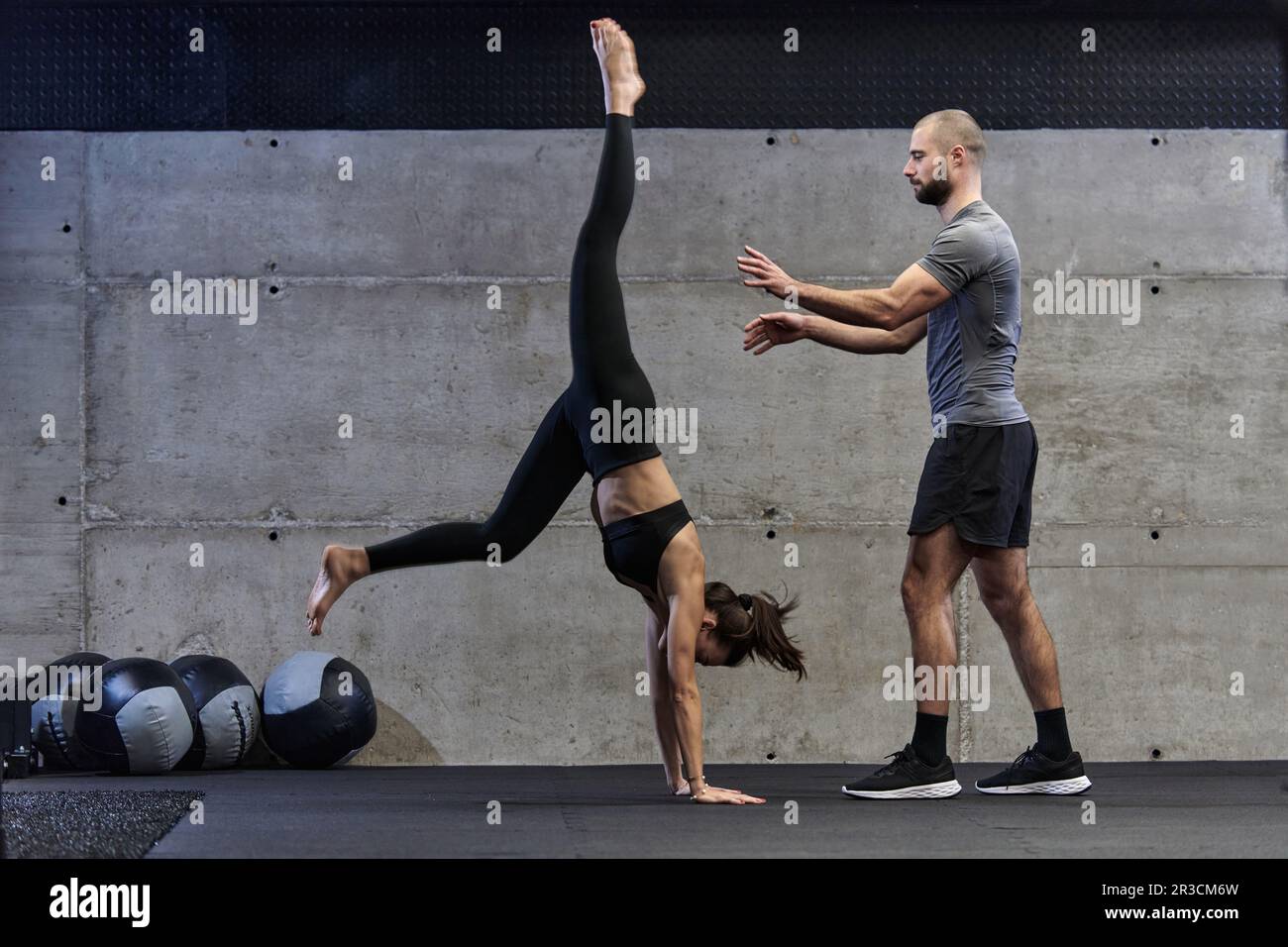 A muscular man assisting a fit woman in a modern gym as they engage in ...