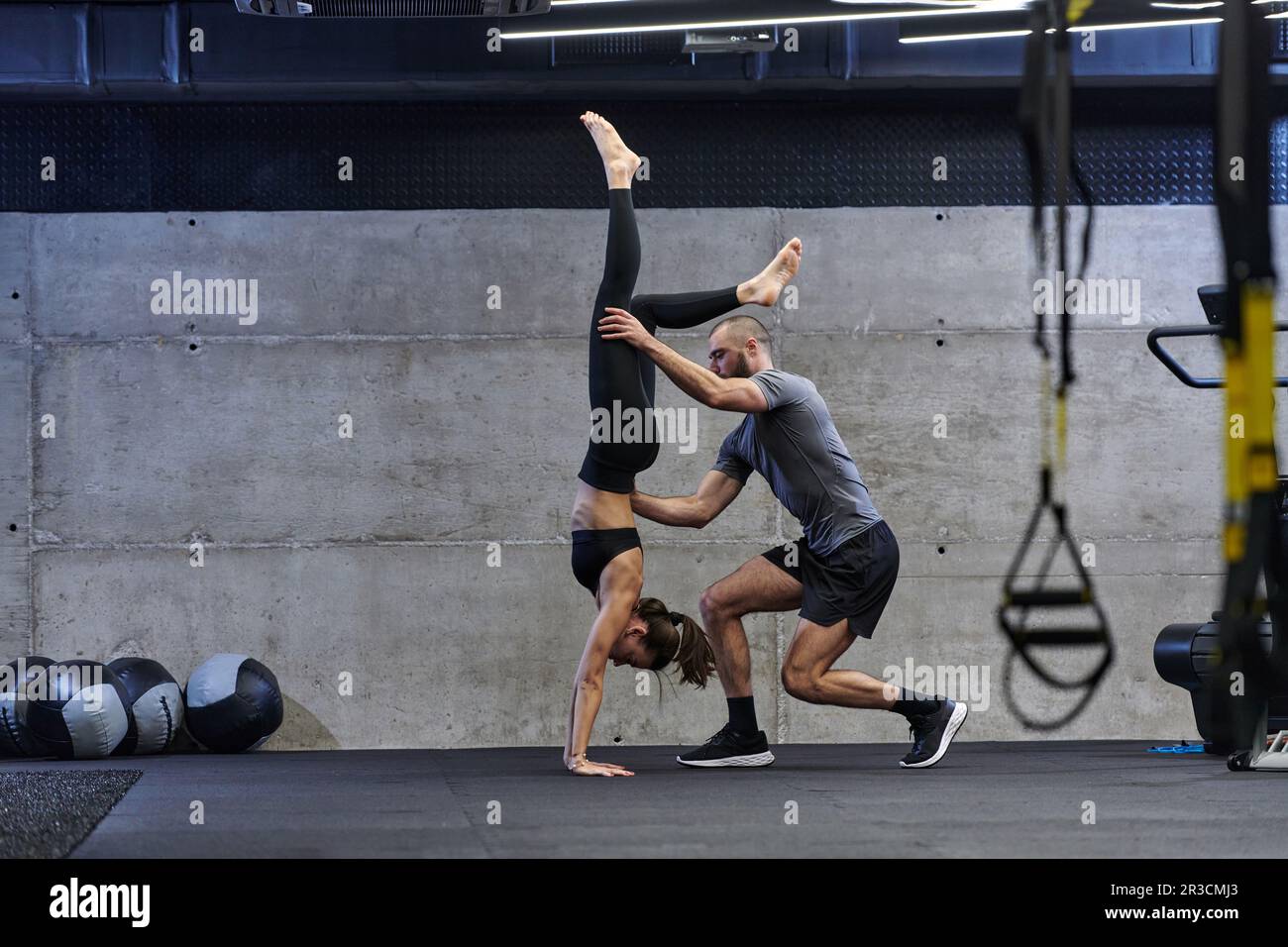 A muscular man assisting a fit woman in a modern gym as they engage in ...